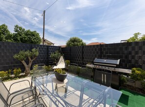 Quintal com mesa de vidro, cadeiras, poltrona suspensa, churrasqueira e cerca preta.