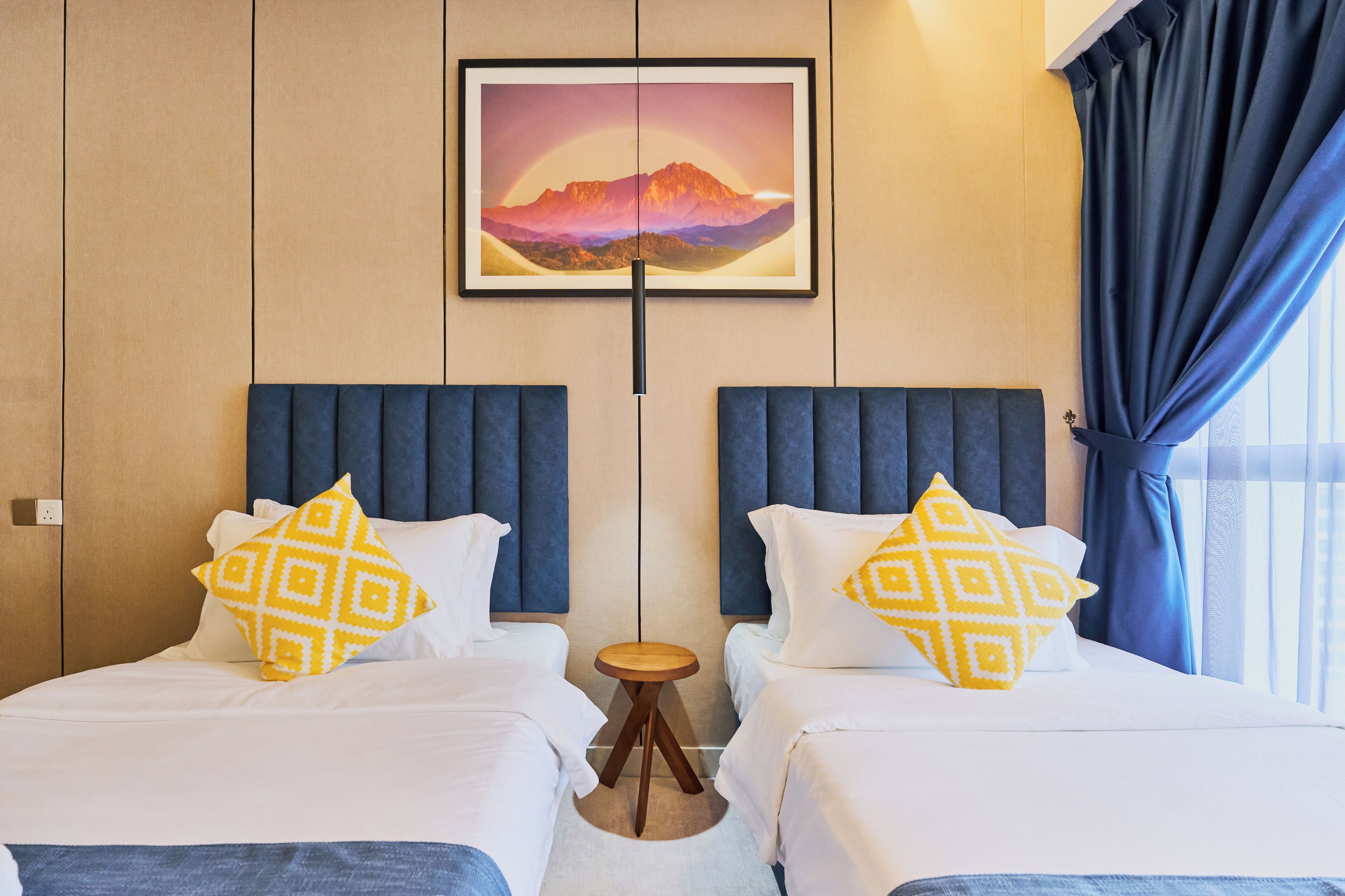 Quarto de hotel com duas camas, uma mesa redonda pequena e um quadro de uma montanha na parede.