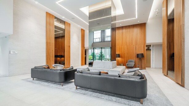 Um hall amplo com design moderno, apresentando um sofá modular cinza, um sofá branco e uma parede de destaque em madeira.