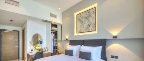 Quarto de hotel moderno com uma cama grande, mesa de cabeceira e guarda-roupa.