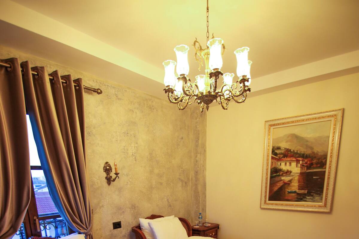 Quarto de hotel com duas camas de madeira, um candelabro, um quadro na parede e vista para o exterior pela janela.