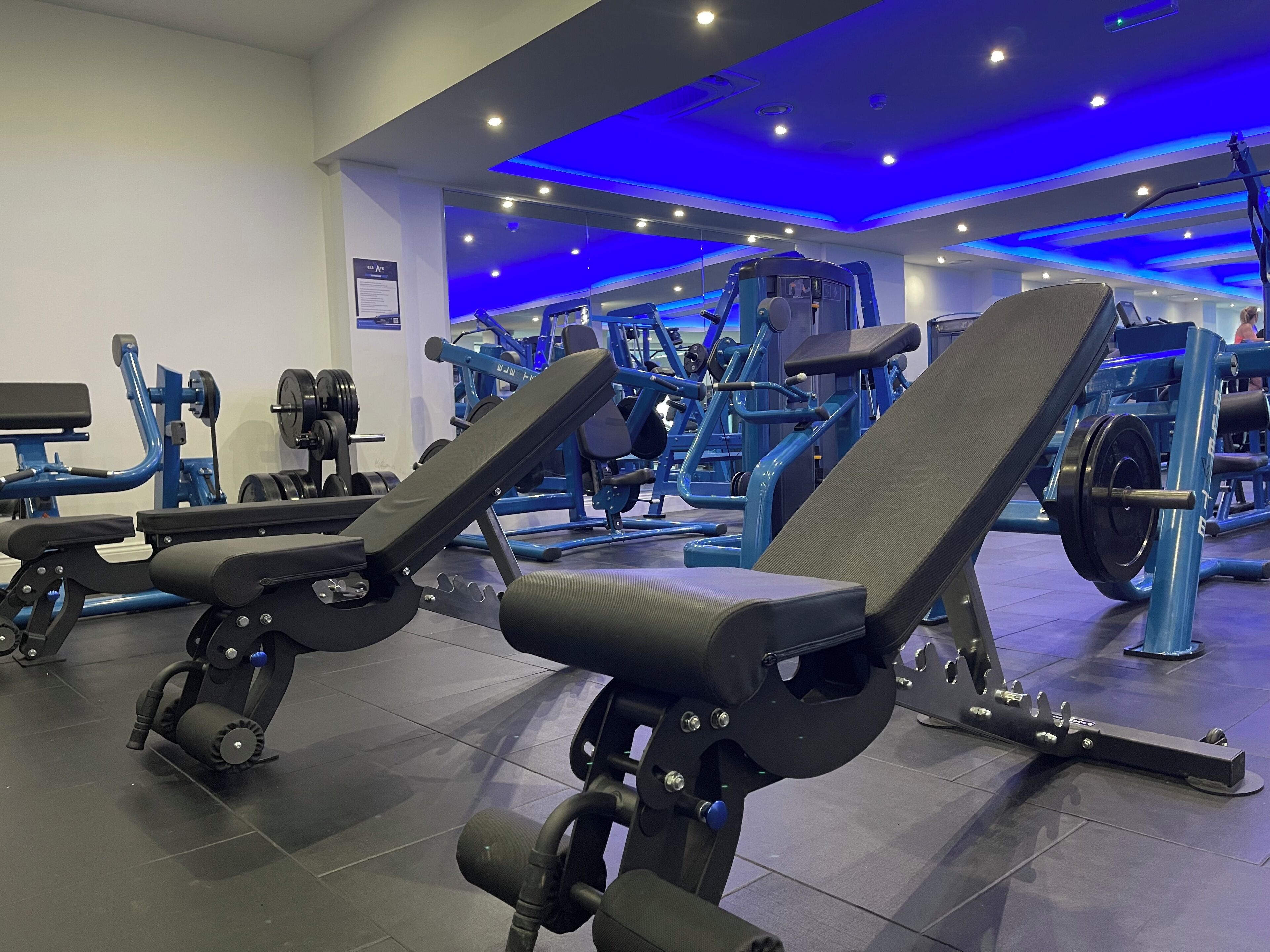 Uma academia com diversos equipamentos de exercício, incluindo bancos de peso e aparelhos.