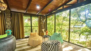 Quarto com janelas amplas, teto de madeira e bean bags listrados.