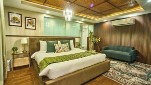 Quarto de hotel moderno com uma cama grande, um sofá, um candelabro e uma janela ampla.