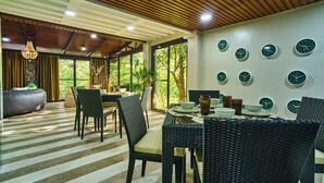 Uma sala de jantar com uma mesa comprida, cadeiras de vime e uma parede com relógios.