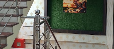 Escada com corrimão de metal, extintor de incêndio vermelho e parede com painel de grama artificial.