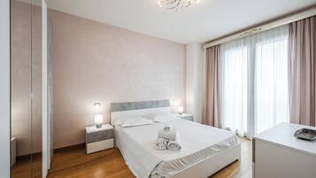 Quarto de hotel moderno com uma cama grande, mesas de cabeceira, escrivaninha e um candelabro.
