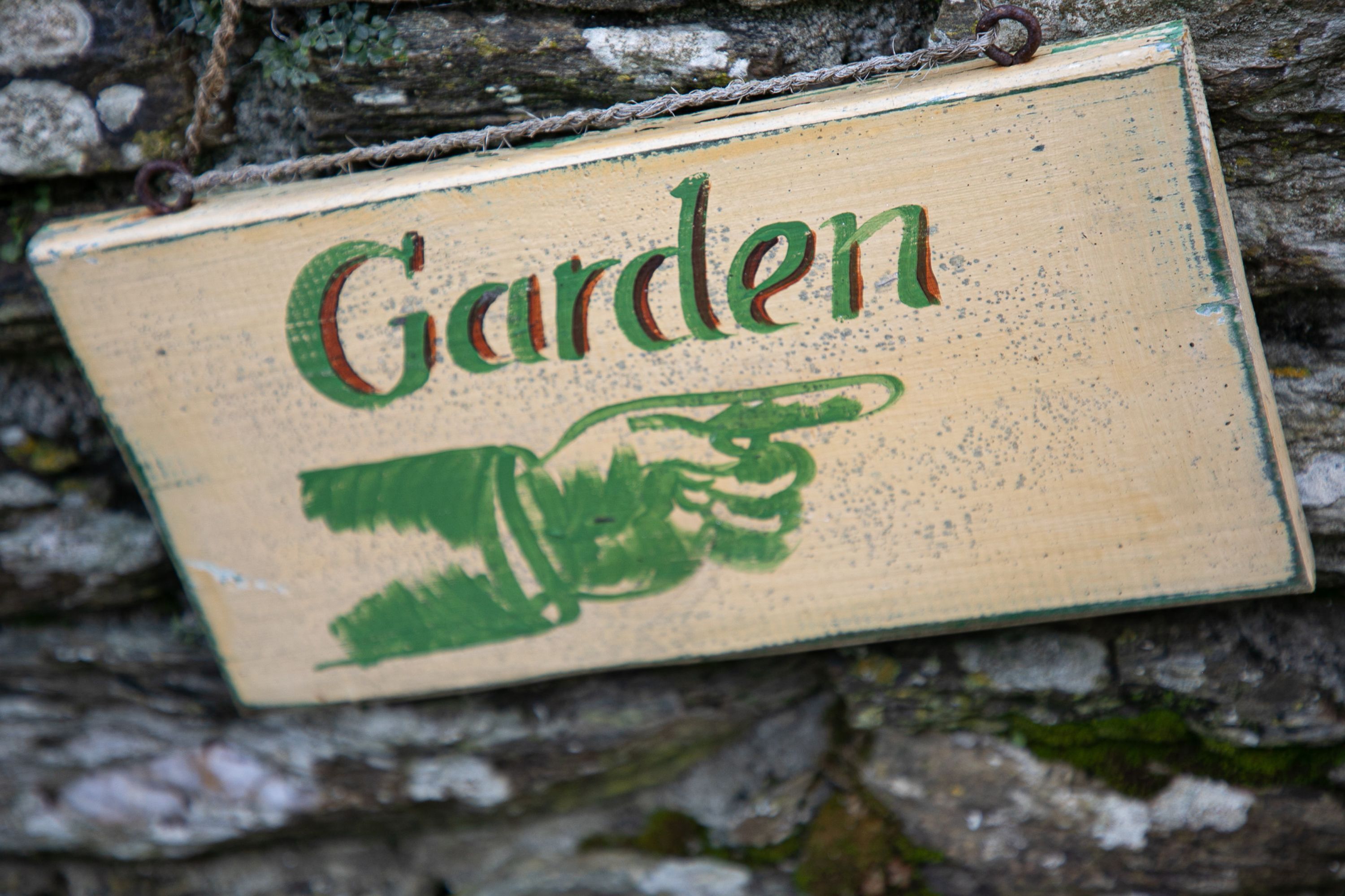 Placa de madeira com a palavra 'Garden' e uma mão apontando para uma planta.
