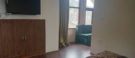 Quarto com cama, guarda-roupa, televisão e janela com cortinas.