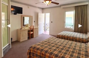 Quarto de hotel com duas camas, uma escrivaninha com cadeira, televisão e uma janela grande com cortinas.