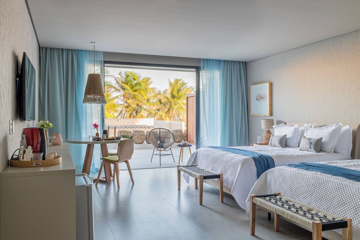 Quarto de hotel com varanda, área de refeições, cama com vista e televisão na parede.