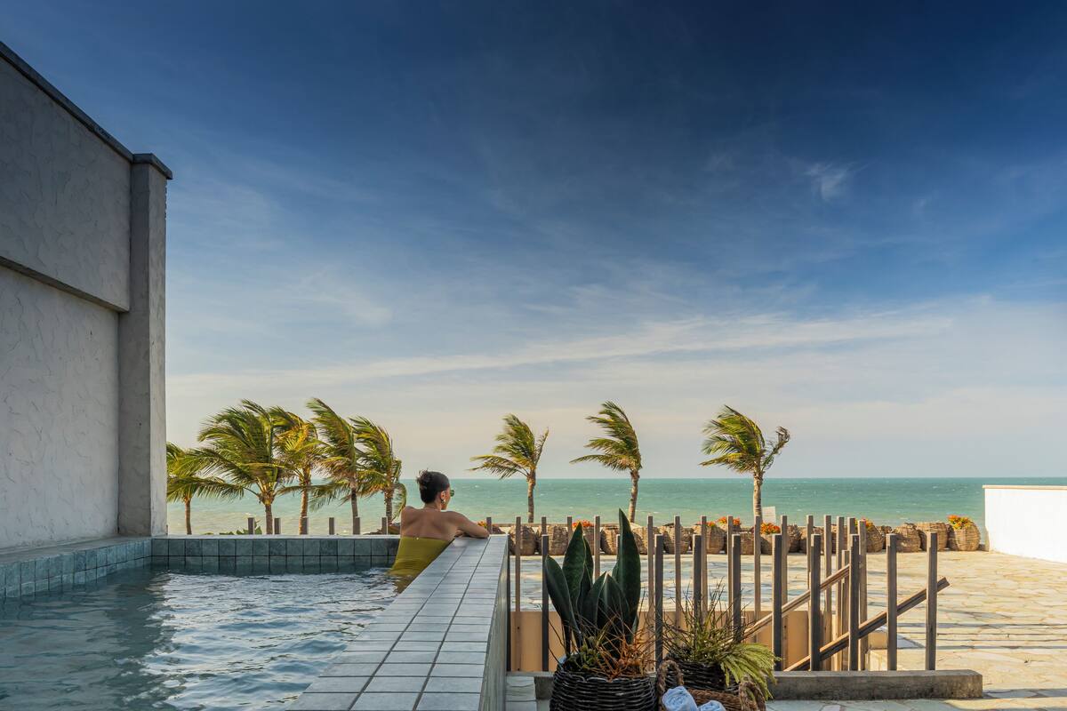 Uma pessoa relaxando em uma piscina com vista para o oceano e palmeiras.