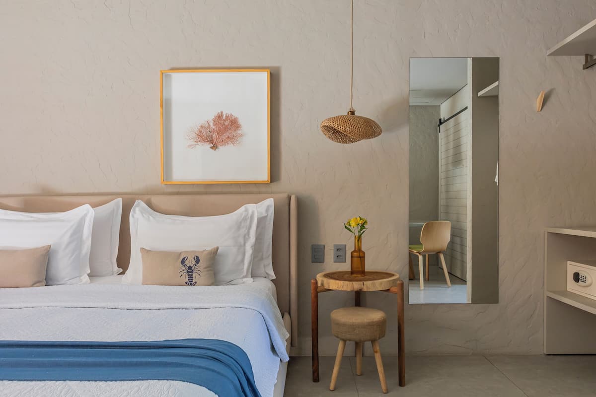 Quarto com cama, mesa de cabeceira com um vaso, espelho e luminária pendente.
