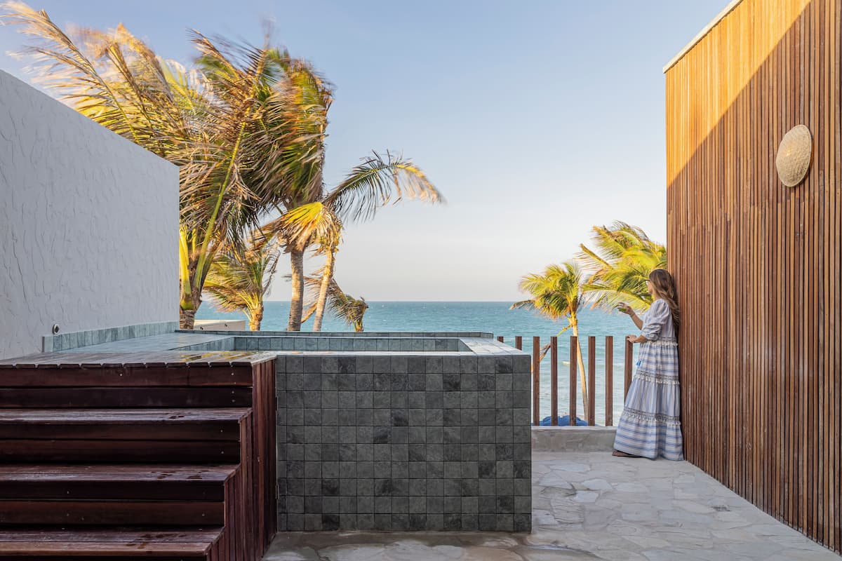 Uma área de piscina com vista para o oceano, escadas de madeira e uma pessoa ao lado da piscina.