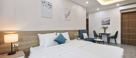 Quarto de hotel moderno com uma cama grande, mesa de cabeceira e uma pequena área de trabalho com cadeiras.