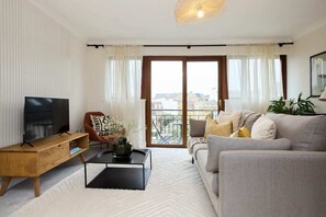 Uma sala de estar moderna com sofá, mesa de centro, televisão e varanda com cortinas.
