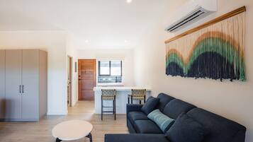 Uma sala de estar moderna com um sofá, uma mesa redonda e uma cozinha ao fundo.