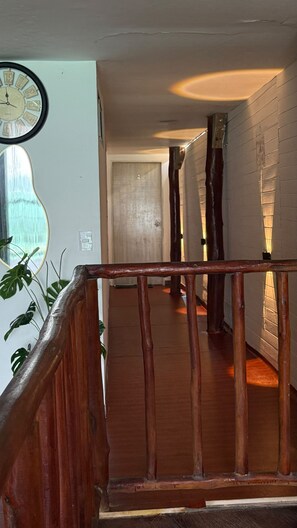 Escada de madeira que leva a uma porta, com um relógio na parede e uma planta à esquerda.