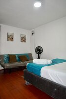 Quarto com cama, sofá, ventilador e duas quadros pendurados na parede.