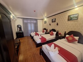 Quarto de hotel com duas camas, piso de madeira, espelho, escrivaninha e janela com cortinas.