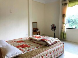 Quarto com cama, mesa de cabeceira, espelho, ventilador e janela com cortinas.