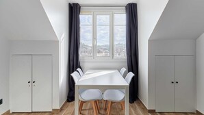 Quarto com uma mesa e cadeiras brancas, uma janela com cortinas e dois armários.