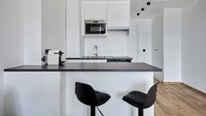 Cozinha moderna com armários brancos, bancada preta e dois bancos altos pretos.