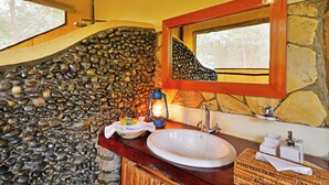 Um banheiro com parede de pedra, toucador de madeira, pia branca, espelho e um candeeiro.