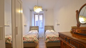 Quarto com duas camas de solteiro, cómoda de madeira, espelho e luminária pendente.