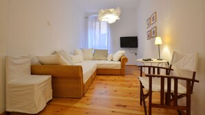 Um quarto pequeno e bem iluminado com um sofá, uma cadeira, uma mesa e uma televisão.