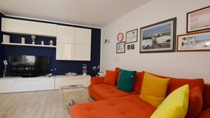 Sala de estar com sofá, televisão e cozinha com armários.