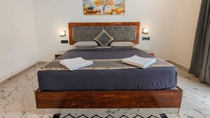 Uma cama com cabeceira de madeira, duas luminárias laterais e um quadro na parede acima.