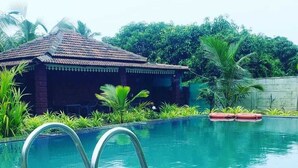 Piscina com escadas de metal, rodeada por vegetação exuberante e um edifício com telhado de azulejos.