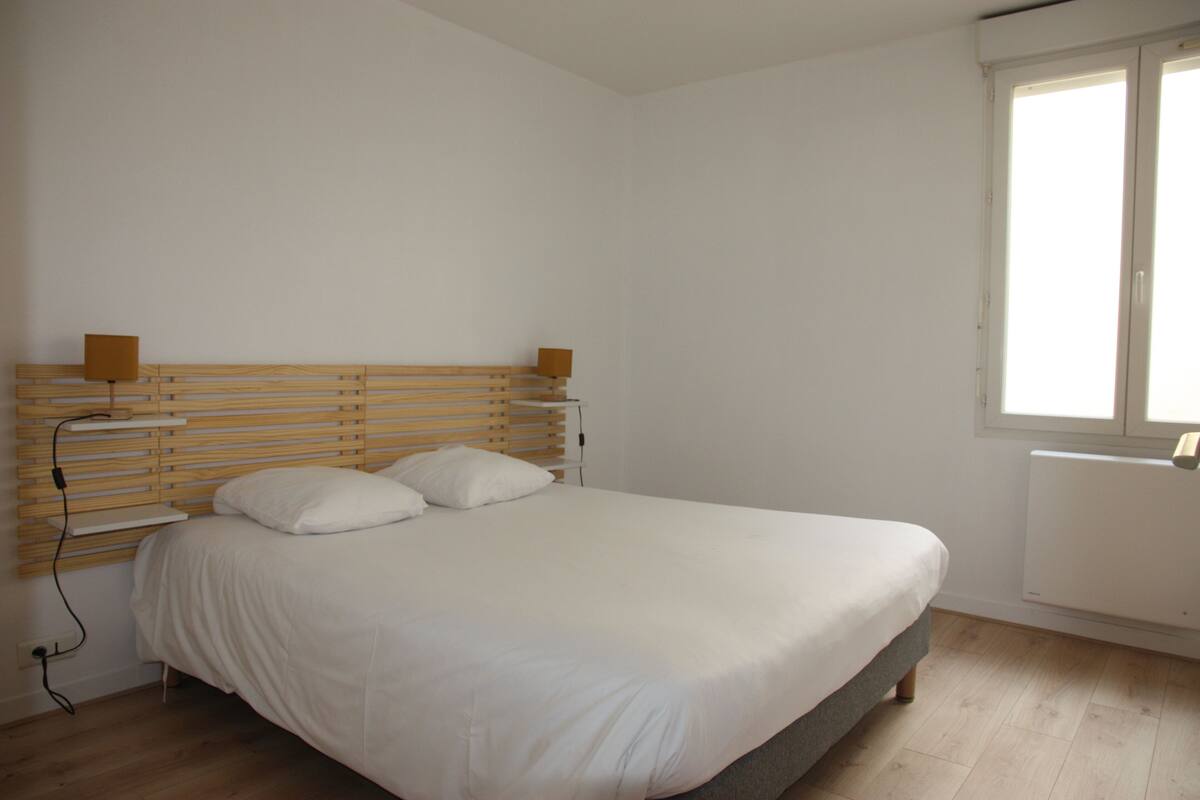 Quarto com cabeceira de madeira, cama com roupa de cama branca e janela com persianas.