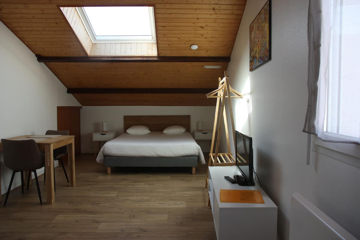 Quarto com claraboia, cama, escrivaninha e guarda-roupa.