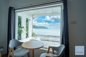 Quarto com vista para o mar, uma mesa redonda, duas cadeiras e uma pequena mesa branca.