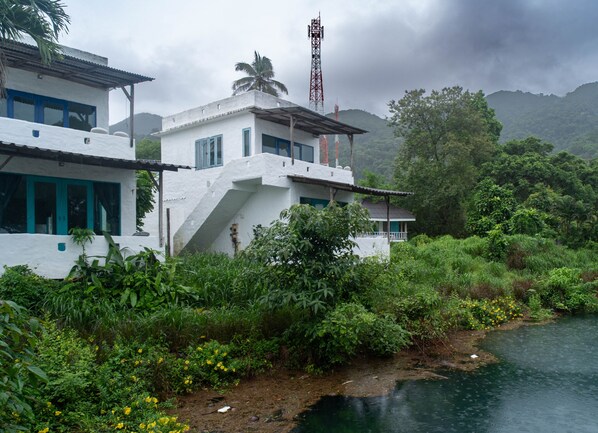 Um edifício branco com detalhes em azul, uma escadaria e vista para um rio e vegetação.
