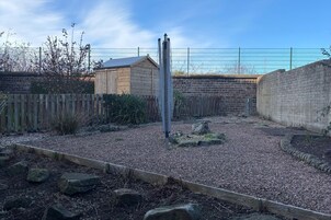 Uma área de jardim com um galpão de madeira, um poste de metal e um muro de tijolos.