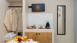 Quarto de hotel com cama, mesa de cabeceira com itens de café da manhã, televisão, cafeteira e espelho.