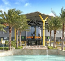 Um edifício moderno com um letreiro 'SUPER FOOD' e área de piscina com palmeiras.