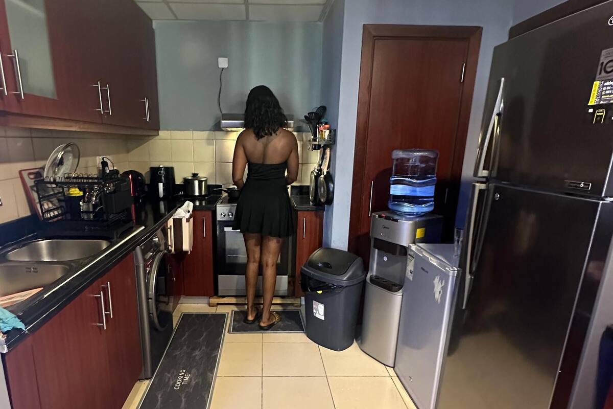 Cozinha com uma mulher em pé no balcão, um bebedouro, uma geladeira e uma lixeira.
