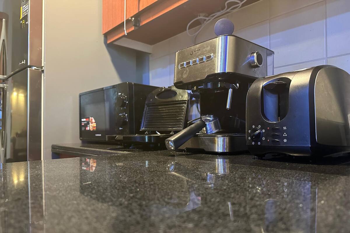 Uma cozinha com máquina de café, micro-ondas e torradeira em bancada de granito.
