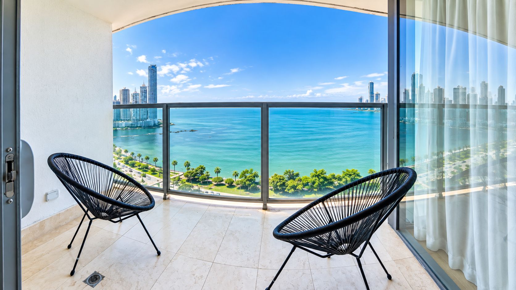 Uma varanda com duas cadeiras, horizonte urbano e vista para o oceano.