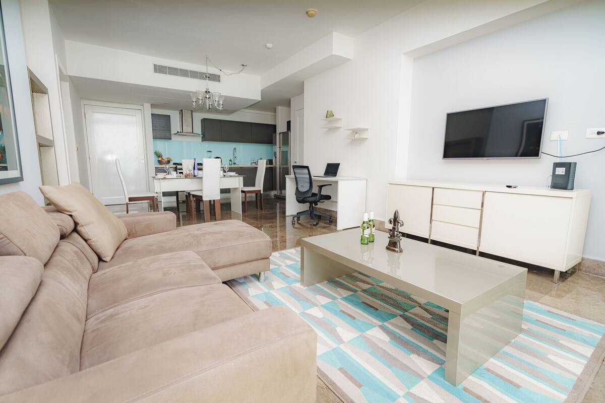 Uma sala de estar moderna com um sofá modular bege, uma mesa de centro e uma TV fixada na parede.