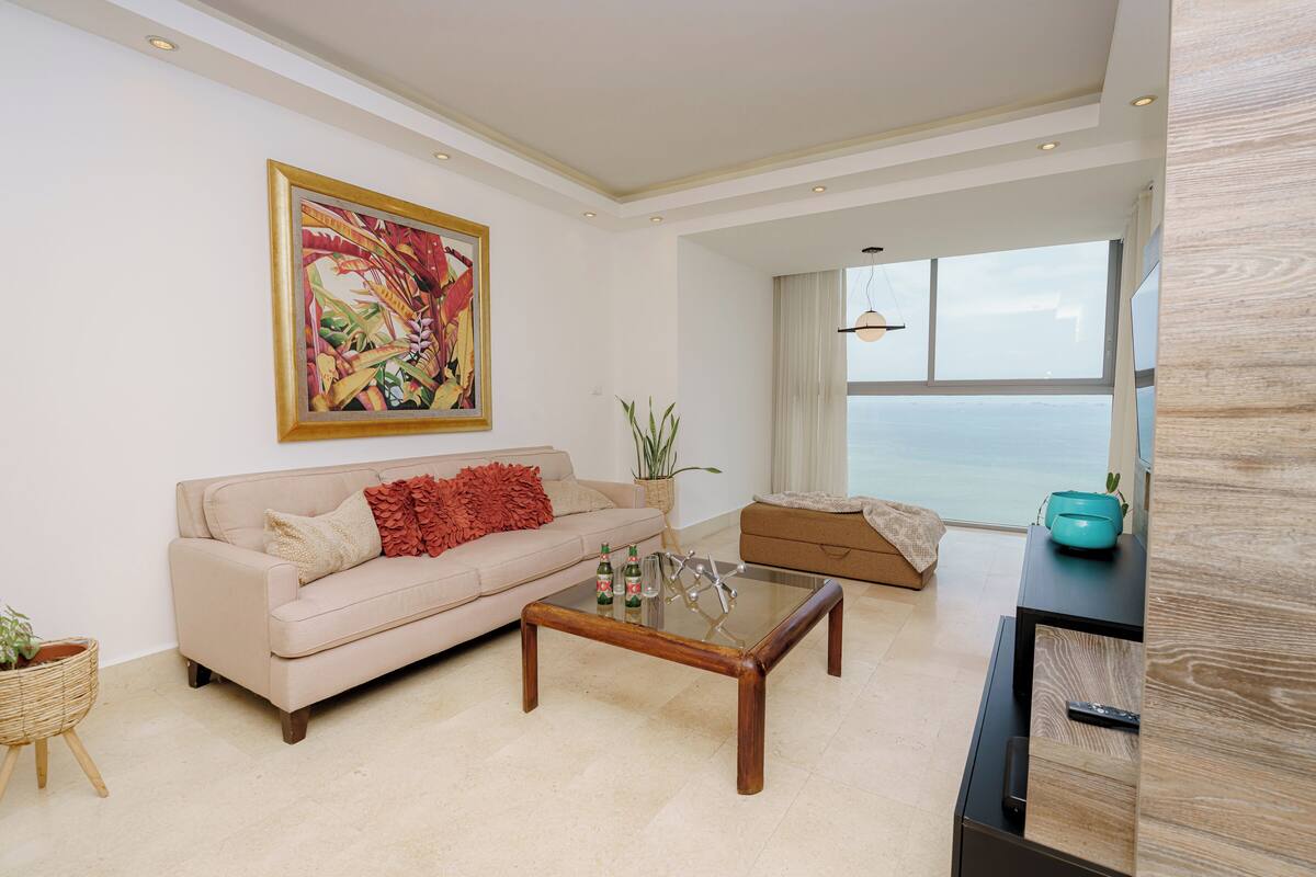 Sala moderna com sofá, mesa de centro e uma grande janela com vista para o mar.