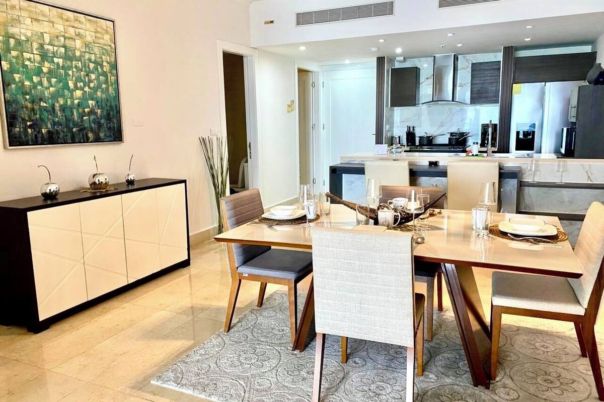 Uma sala de jantar moderna com mesa de madeira, cadeiras estofadas cinzas, um armário branco e uma grande pintura abstrata na parede.
