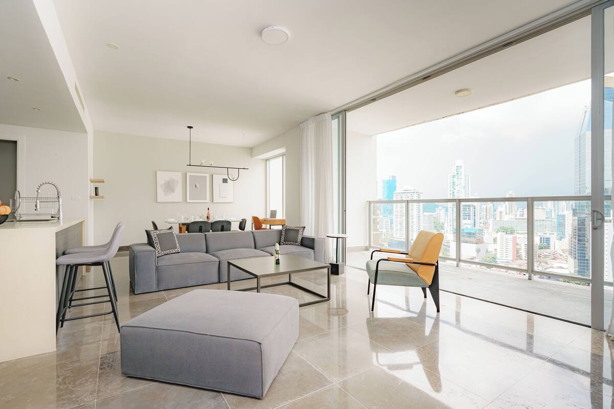 Uma sala de estar moderna com uma janela grande, um conjunto de sofás, uma mesa de centro e um espaço de jantar.