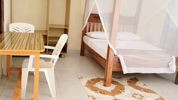 Quarto com cama de madeira, dossel branco, mesa com cadeiras e tapete estampado.