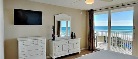Quarto com cama, cômoda, espelho e ventilador de teto. Possui varanda com vista para a praia.