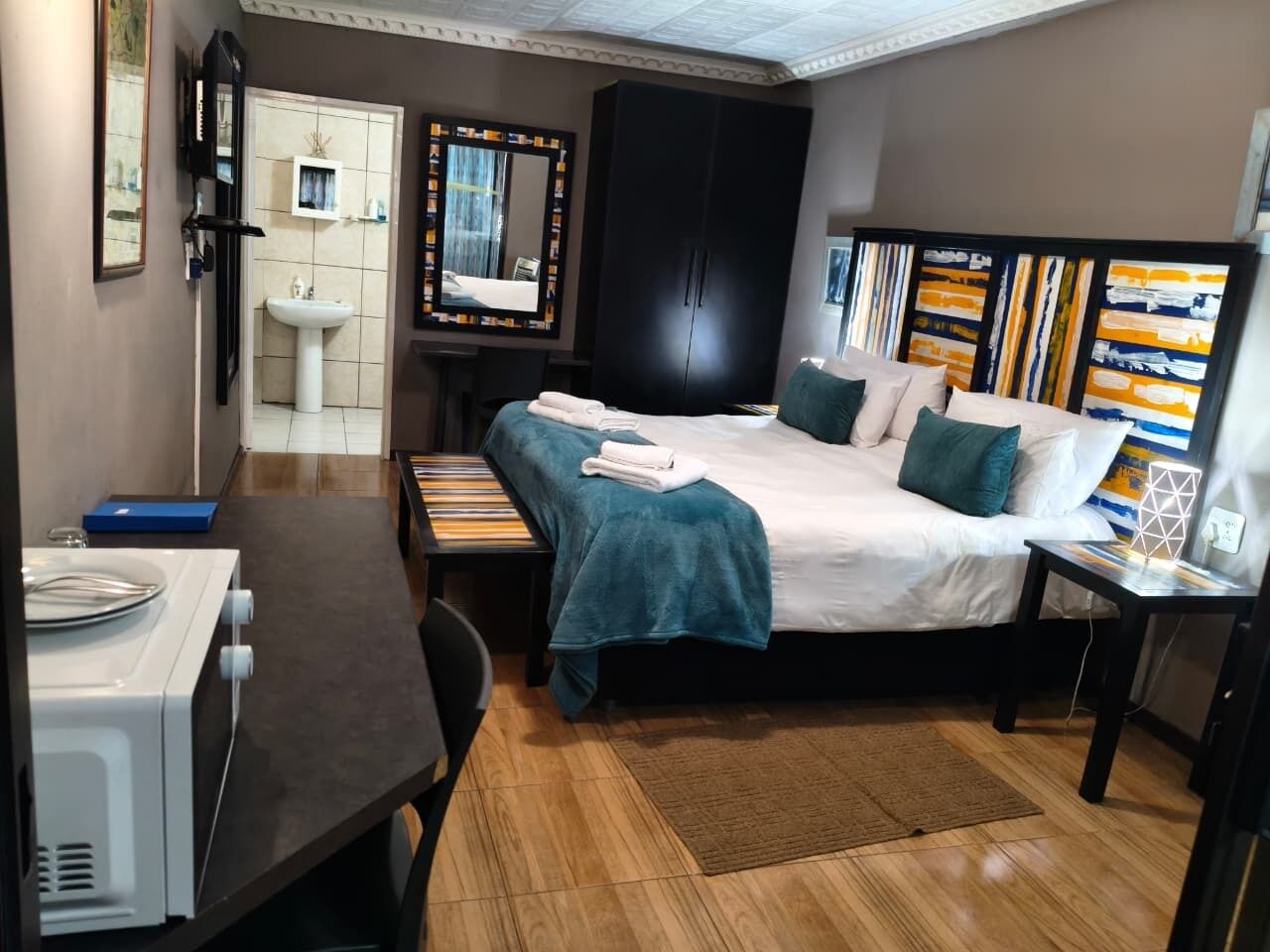 Quarto de hotel com cama, mesa de cabeceira, escrivaninha, máquina de lavar, espelho e armário.